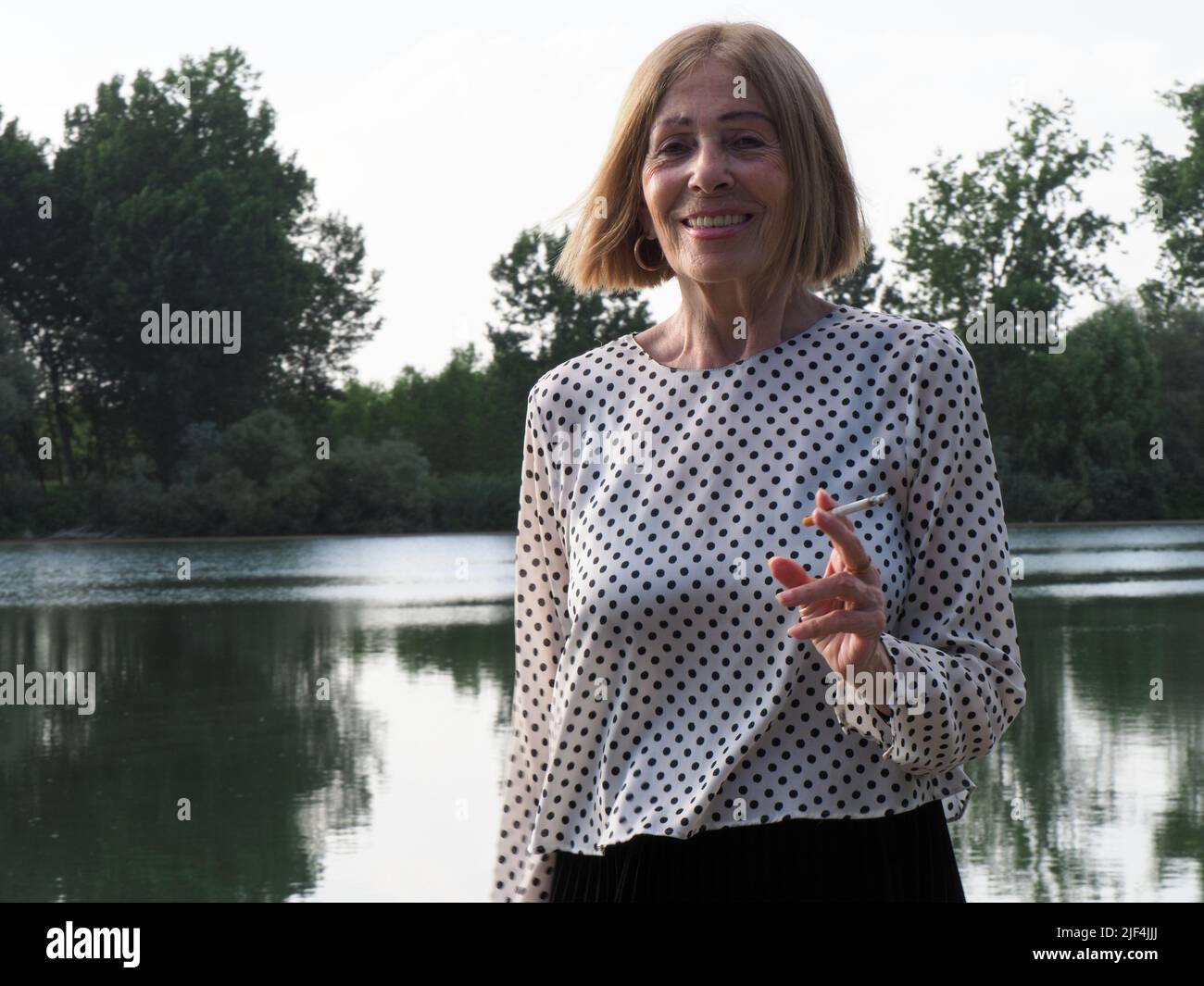 female pensioner having fun and smoking a cigarette in a park - aging ...