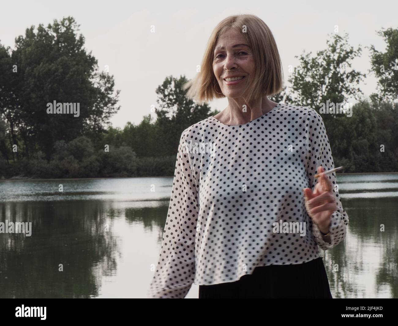 female pensioner having fun and smoking a cigarette in a park - aging ...