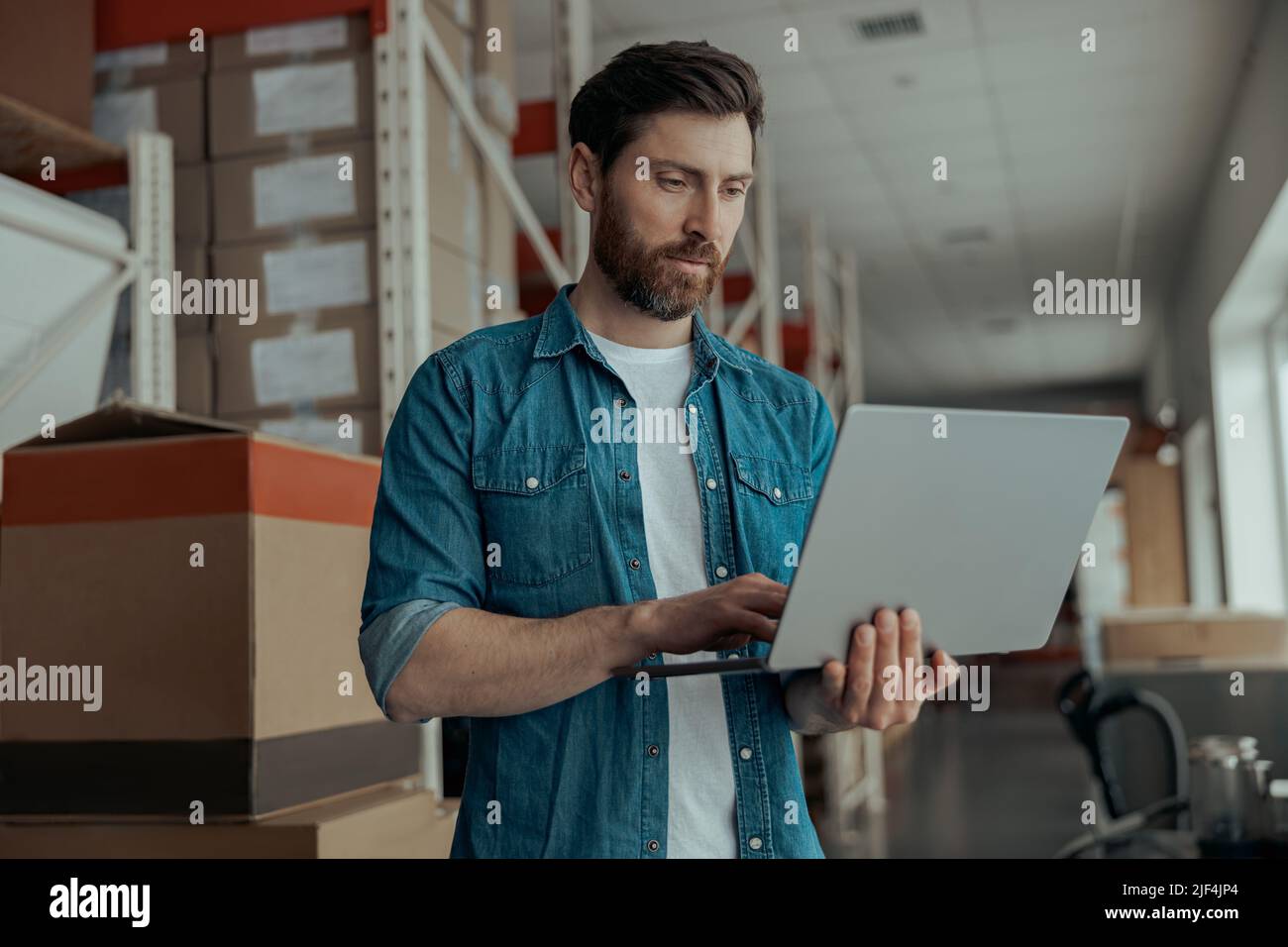 Serious man worker working on laptop stands on warehouse Stock Photo ...