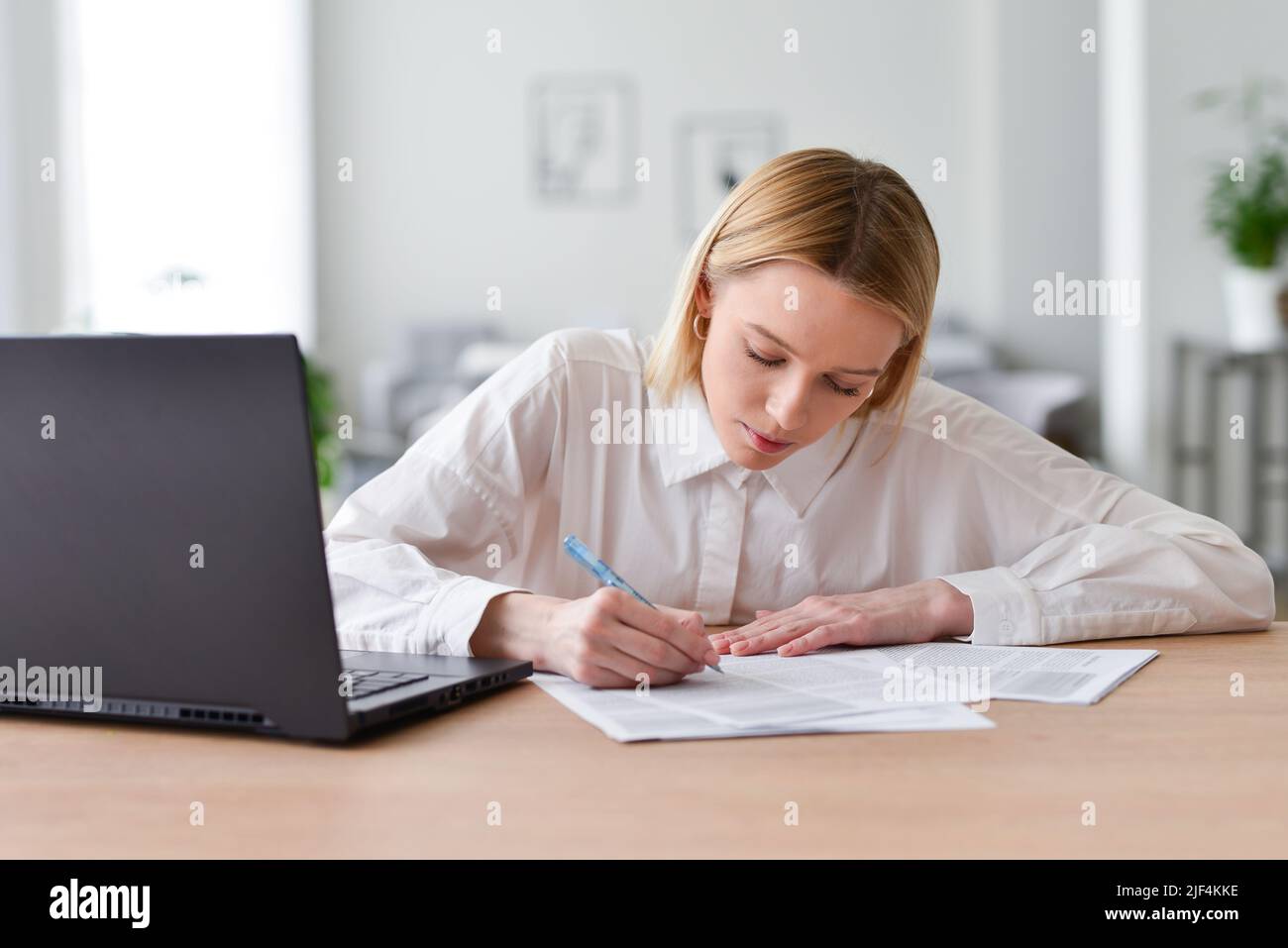 Young woman taking notes on paper while using laptop at home Stock ...