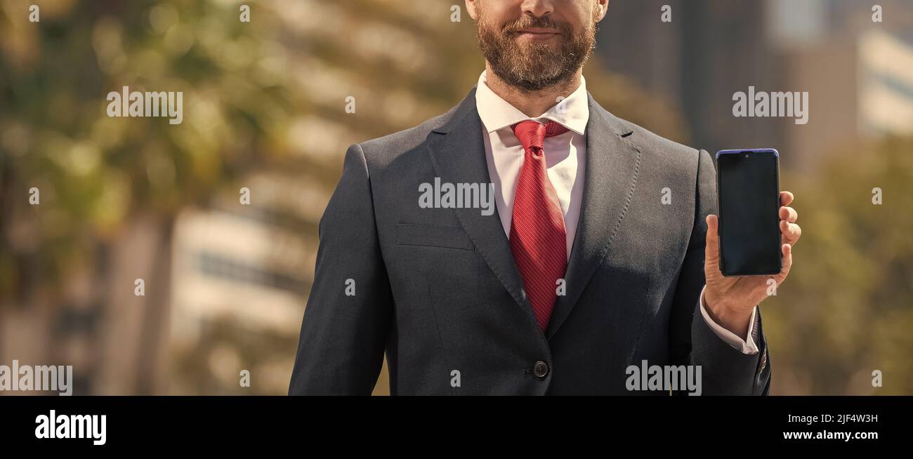 cropped confident man in elegant suit show smartphone screen outside ...