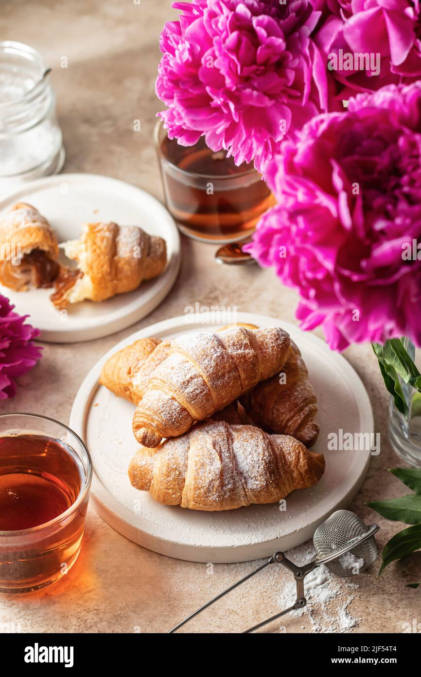 Breakfast with two plates of croissants, tea, sugar bowl and peonies ...