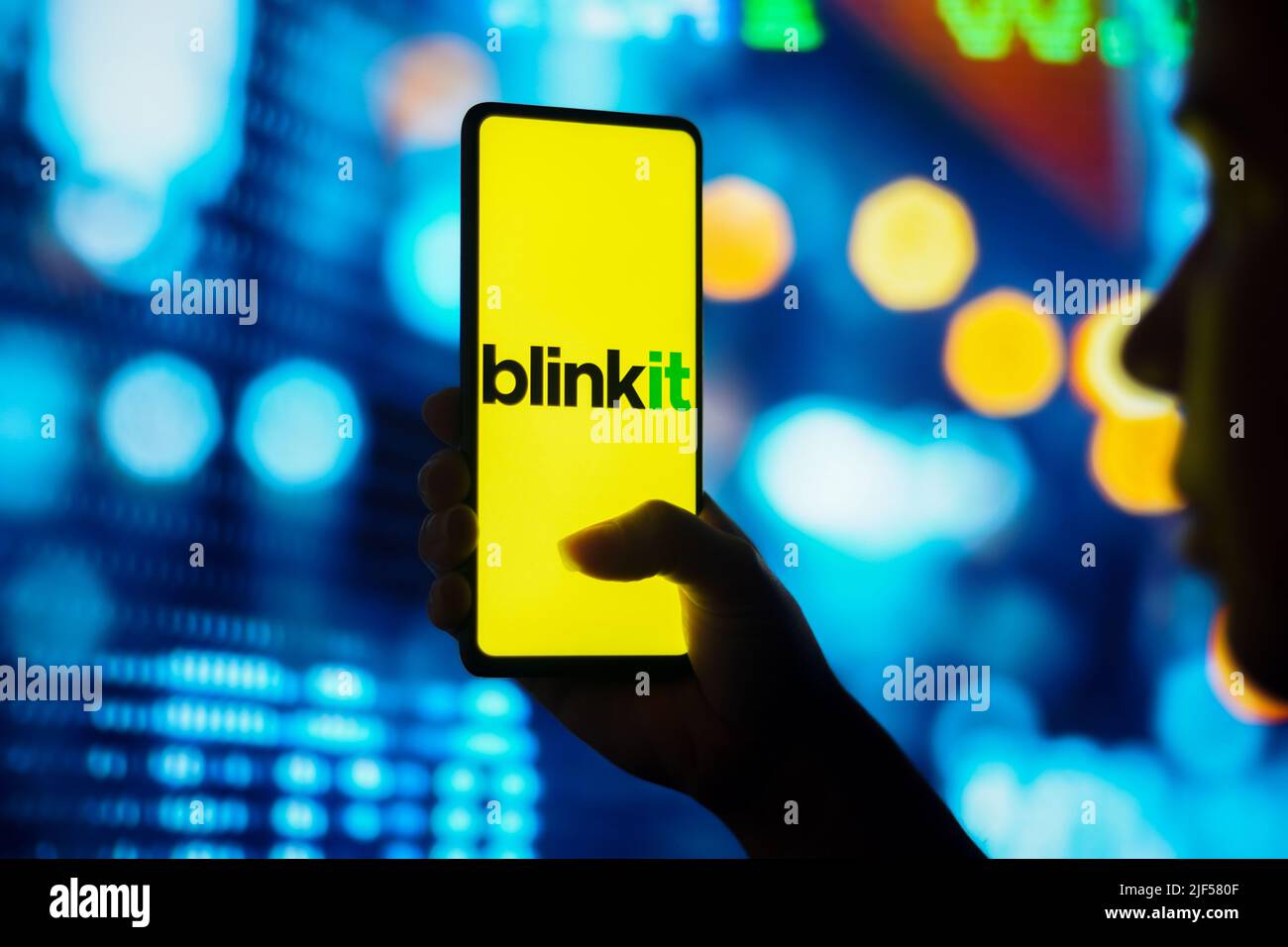In this photo illustration, a silhouetted woman holds a smartphone with the Blinkit logo ...