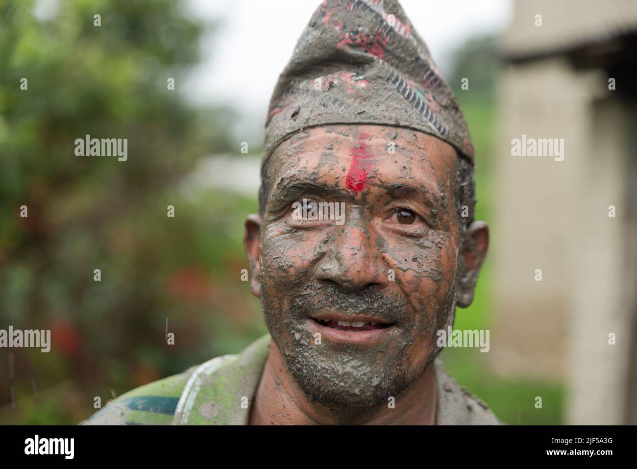 A man's face covered with mud smiles in a rice paddy field during the ...