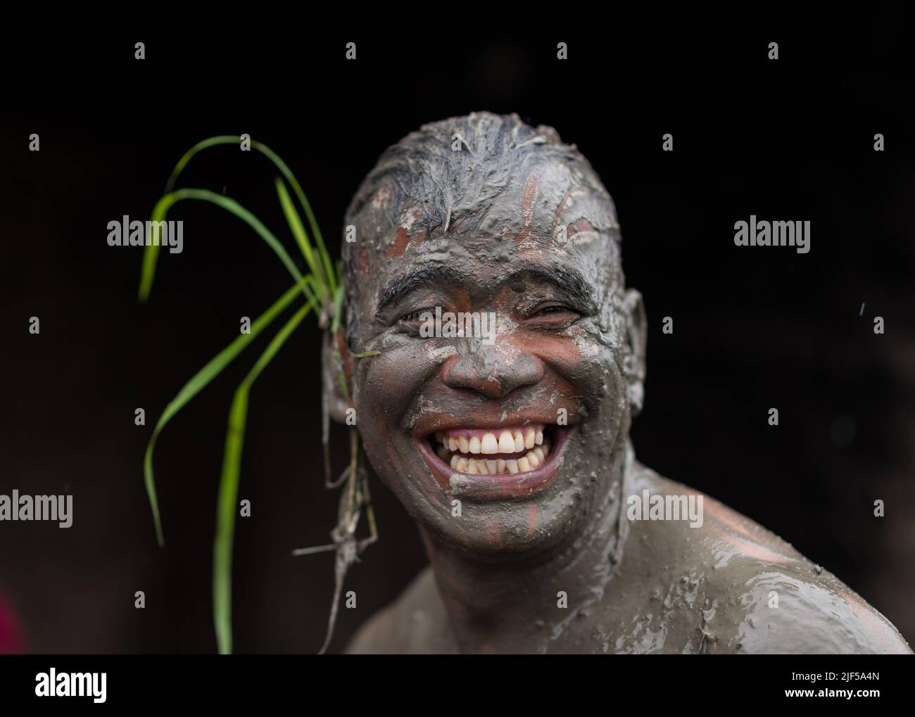 A man's face covered with mud smiles in a rice paddy field during the ...