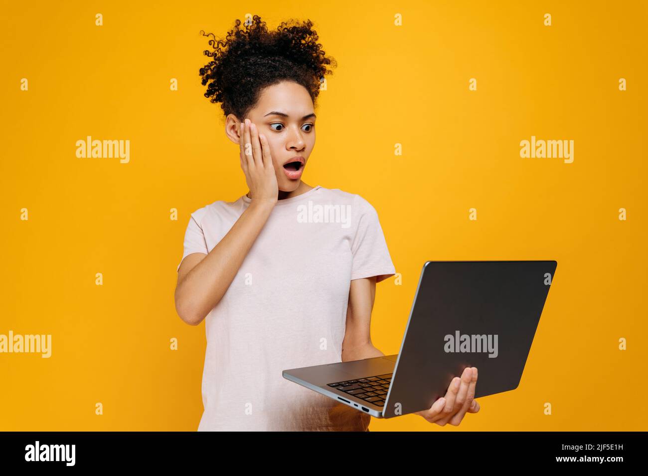 Shocked amazed african american young woman with curly hair, holds an ...