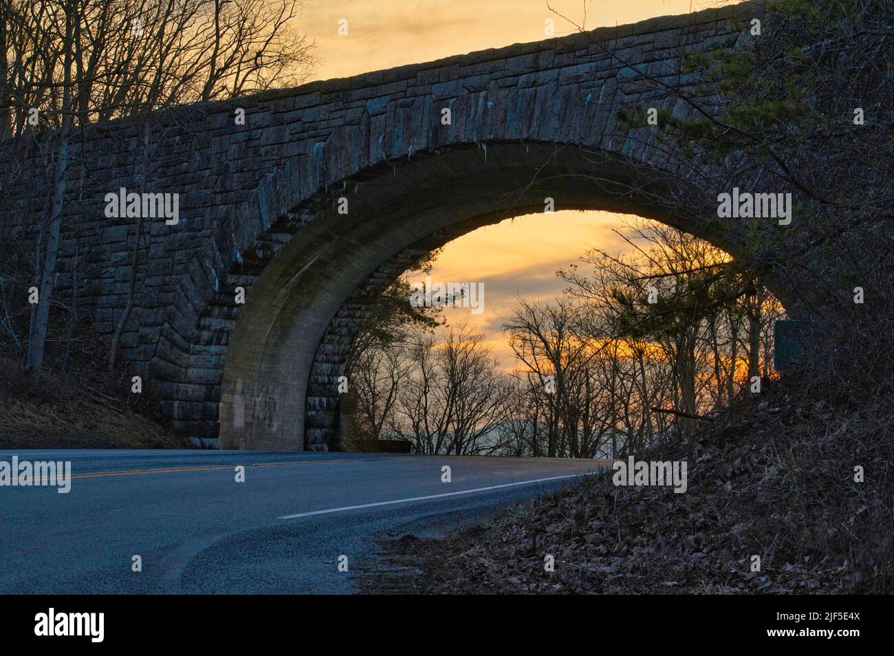 An arched stone bridge over a road under a yellow sunset sky Stock ...