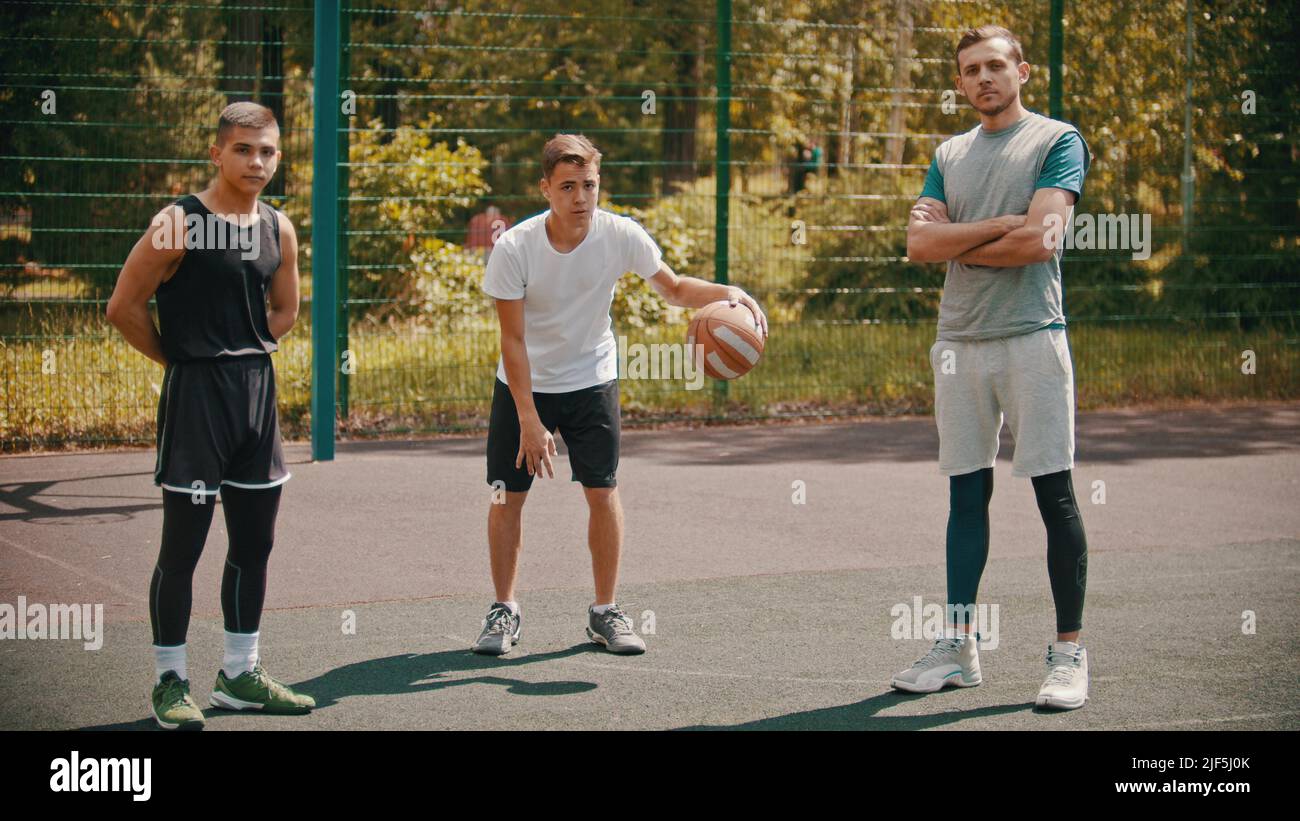 Three sportsmens standing on the basketball court outdoors and looking ...