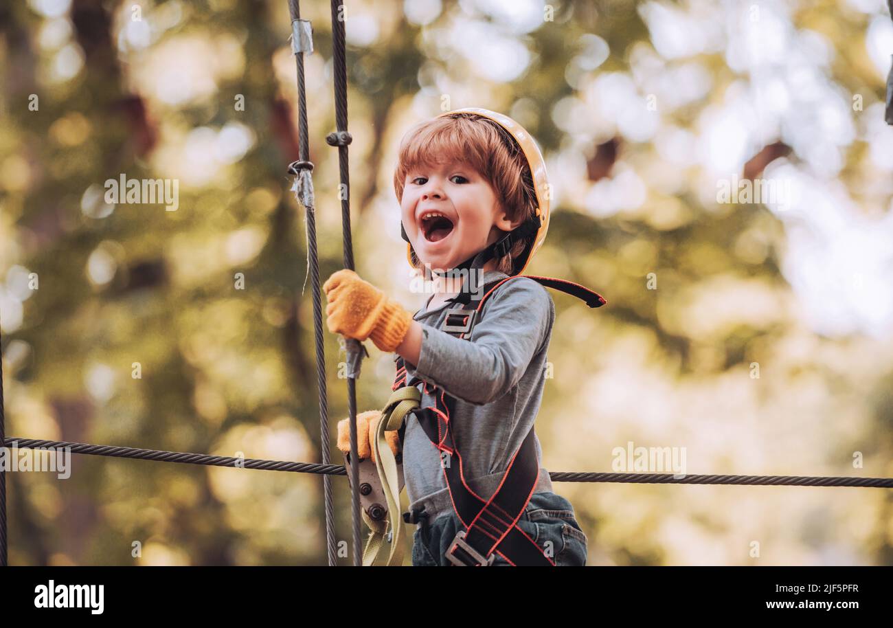 Little child climbing in adventure activity park with helmet and safety ...