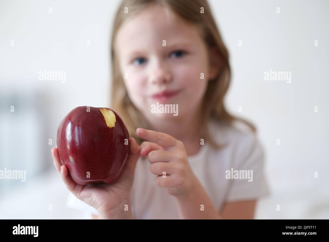 Girl child bites and eats big red apple Stock Photo - Alamy