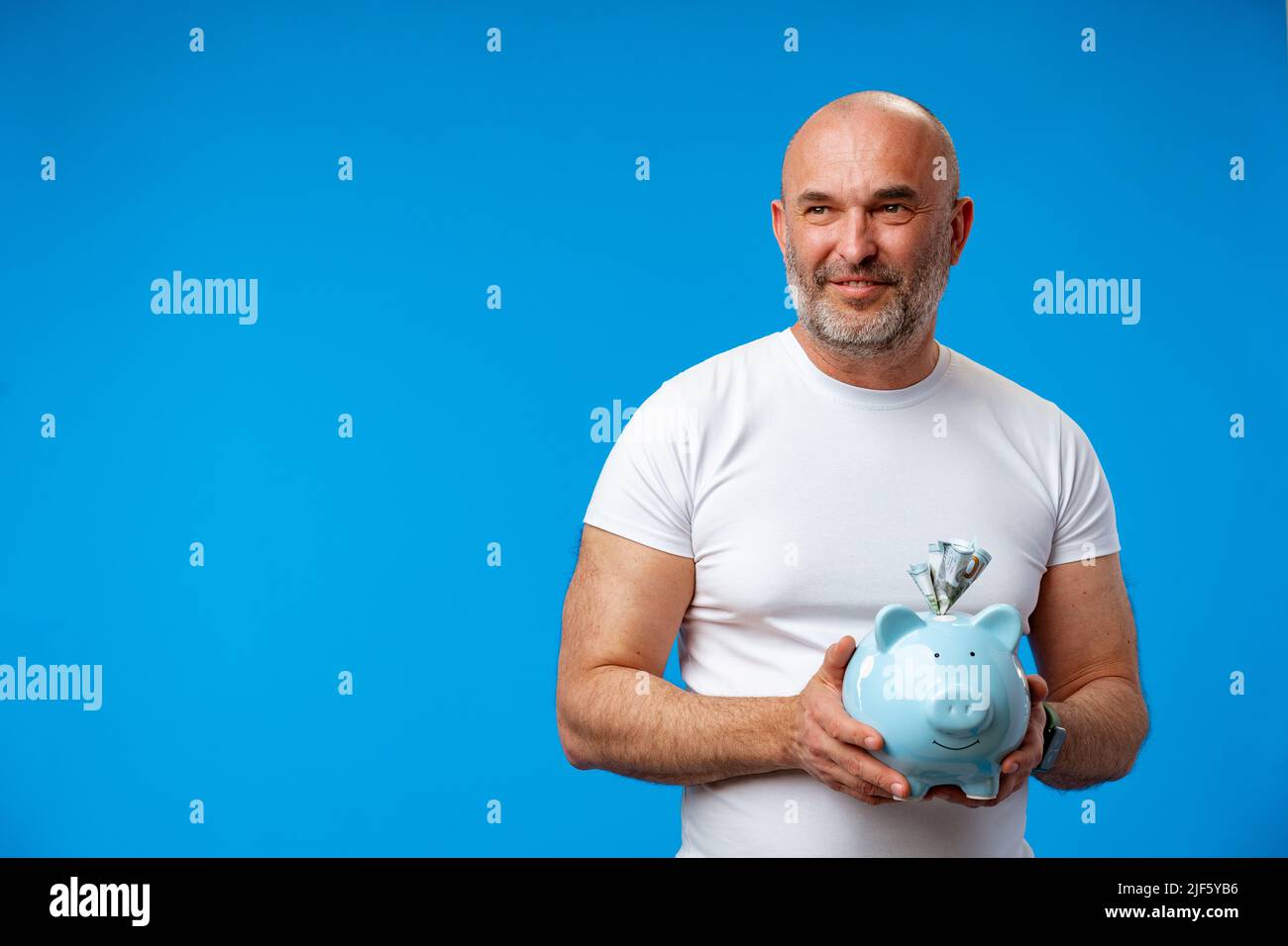 Middle-aged man holding piggy bank against blue background Stock Photo ...