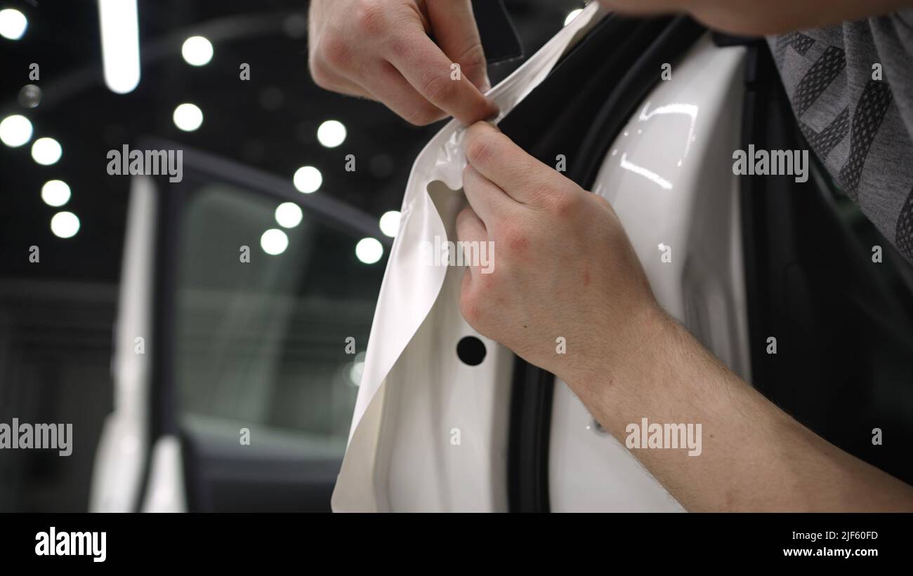 The master sticks a white protective film on the car body. Wrapping a ...