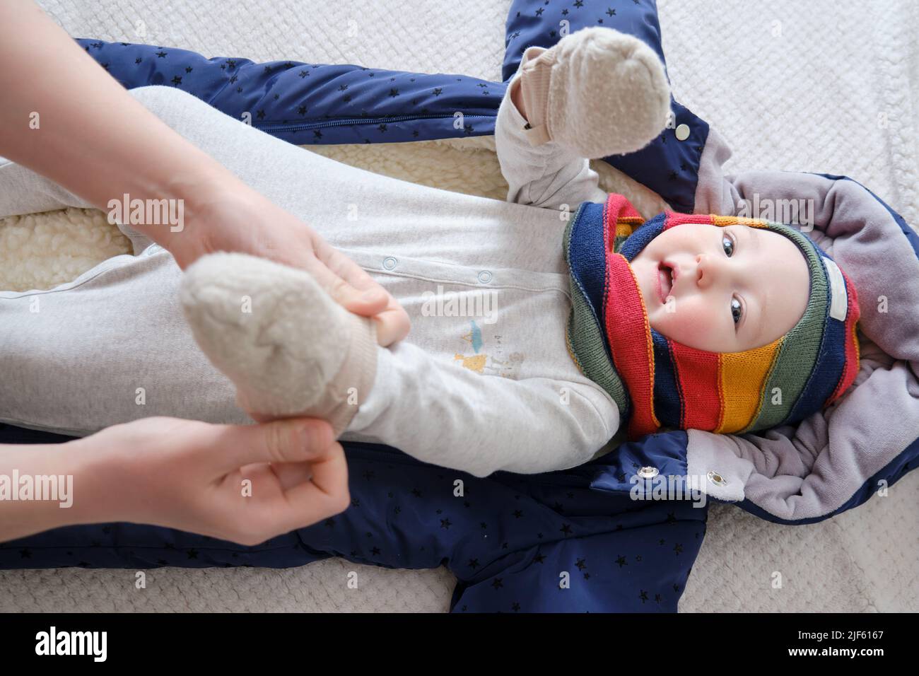 A mother woman puts on warm mittens for a baby boy. Mom dresses a happy ...