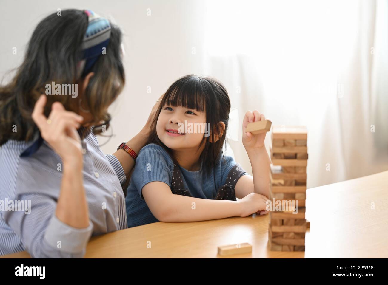Adorable little asian girl enjoy playing wood block stacking board game ...
