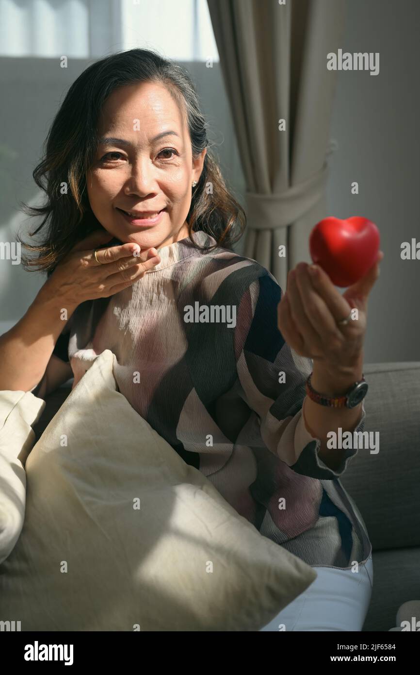 Happy middle aged woman holding heart shape and smiling to camera ...