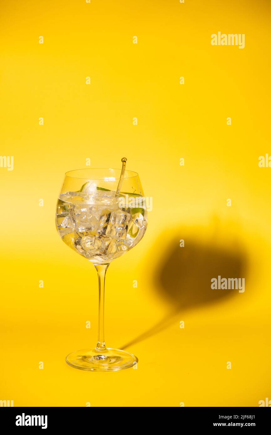 Shadow of a gin glass with gin, tonic and cubes with yellow background ...