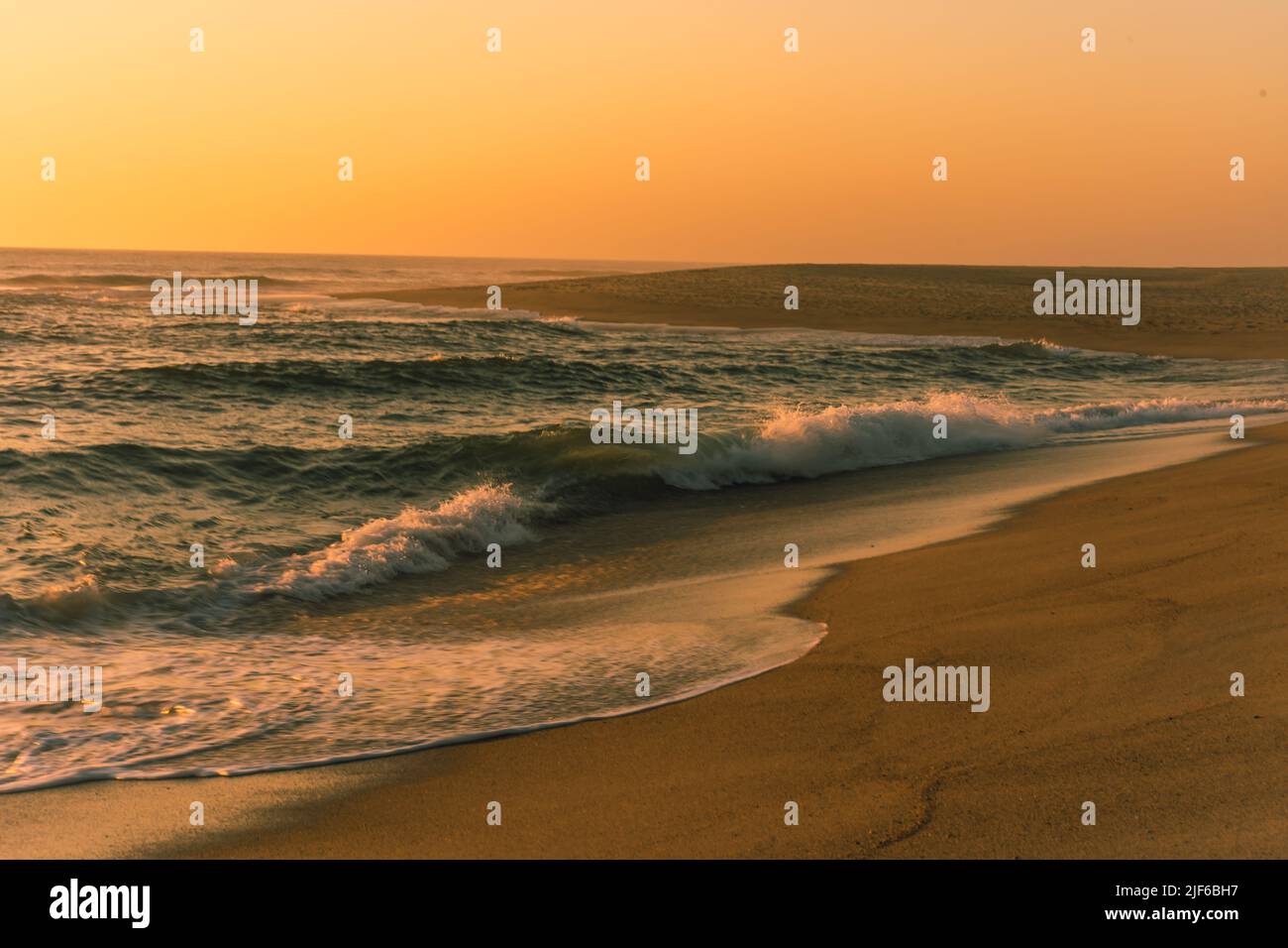 A scenic view of ocean waves crushing against a sandy beach at sunset ...