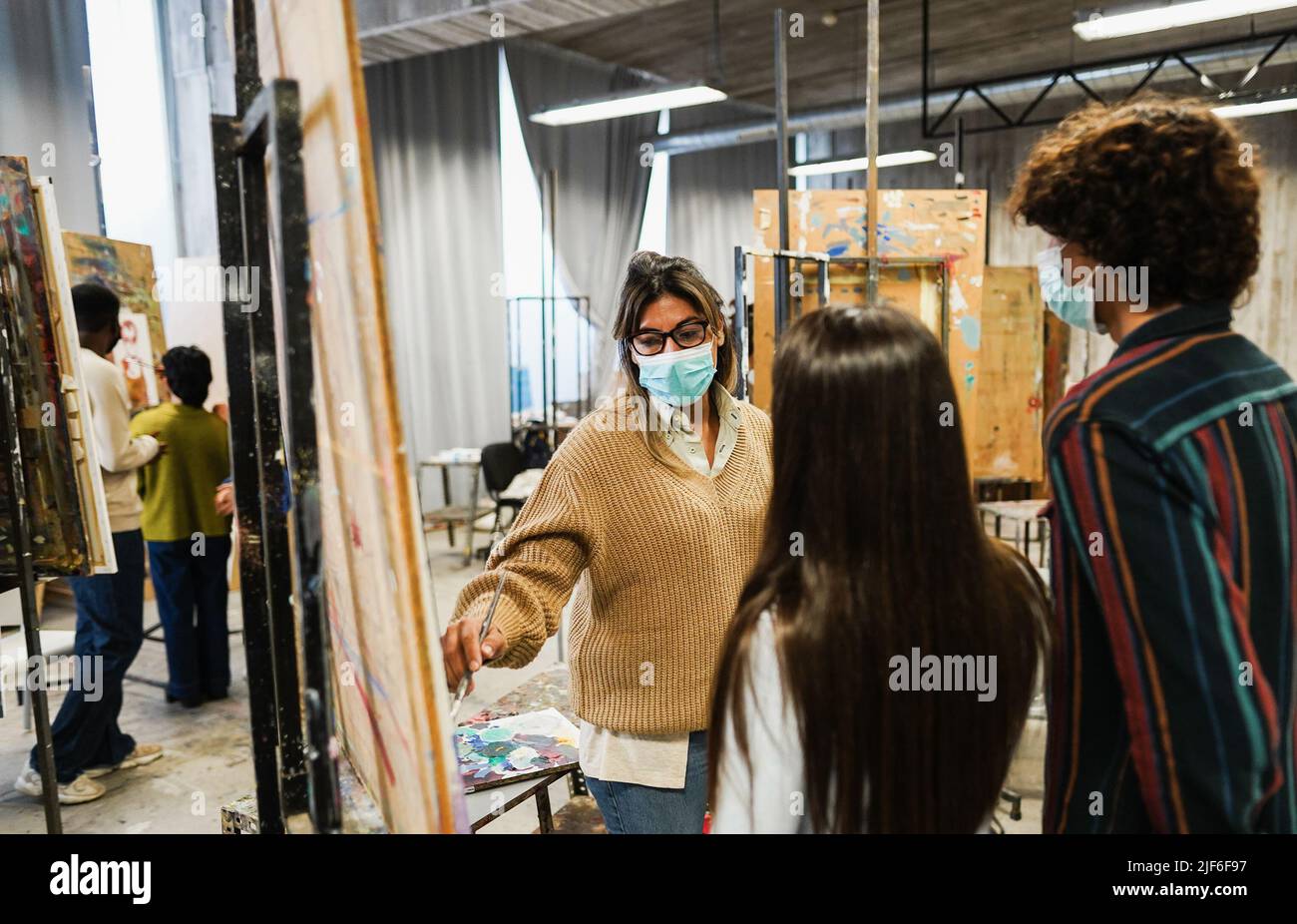 Young students painting inside art room class wearing safety masks ...