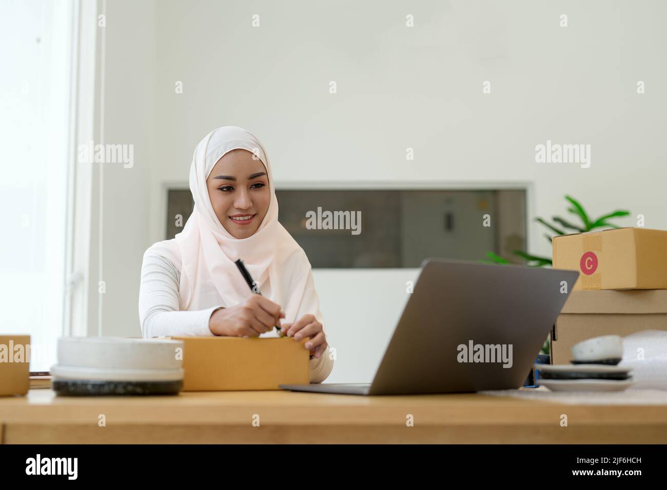 Happy young muslim woman owner writing address on cardboard box, Young ...