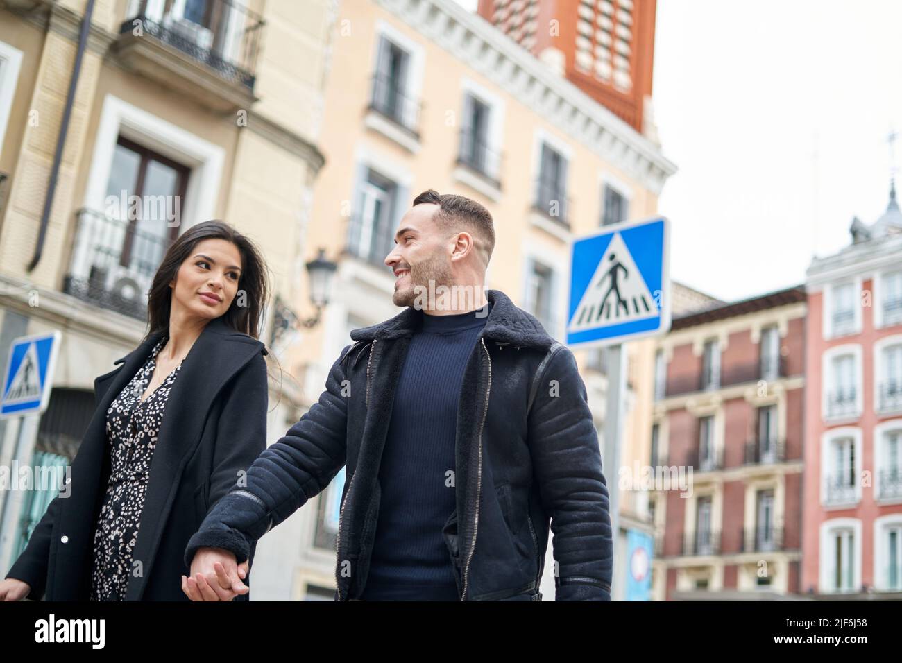 Loving couple in outerwear looking at each other and holding hands ...