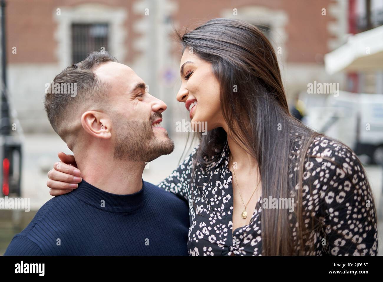 Positive couple in outerwear caressing while standing looking at each ...