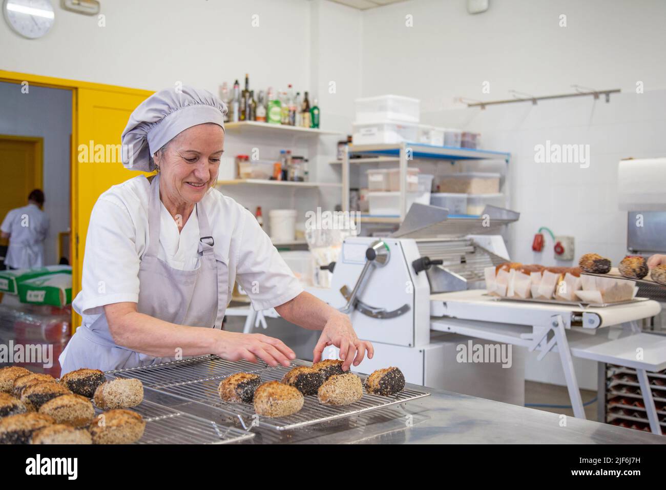 Focused female baker in uniform with baked bread on rack standing at ...