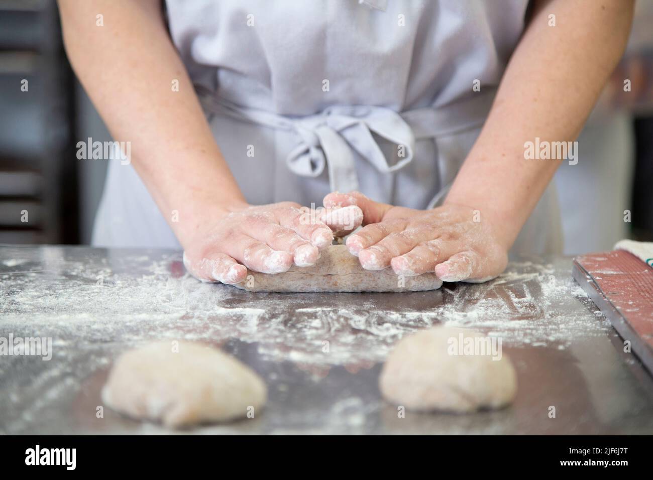 Anonymous female cook in uniform spreading flour on table with balls of ...