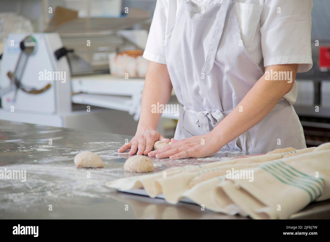 Anonymous female cook in uniform spreading flour on table with balls of ...