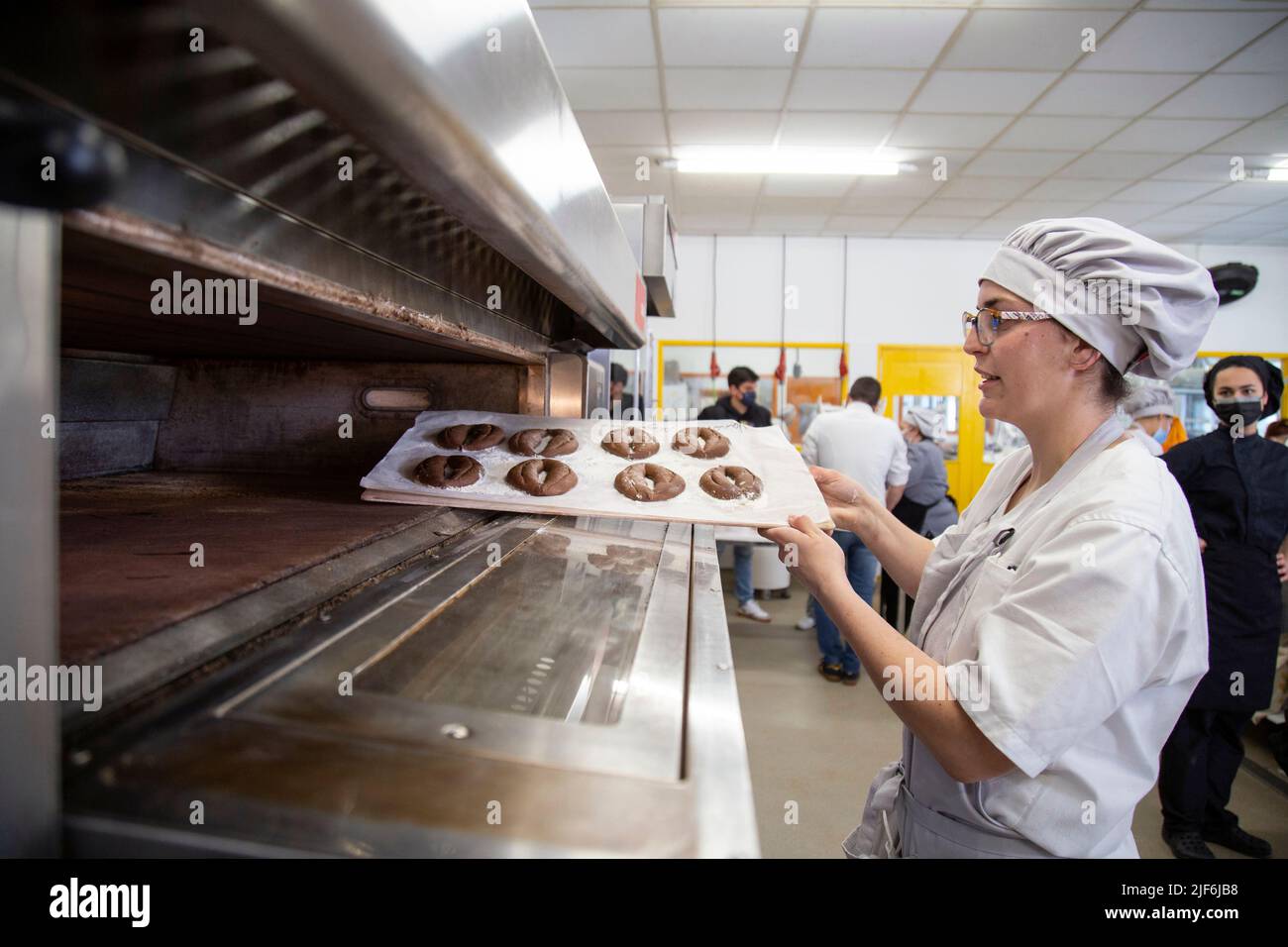 Side view of female baker in uniform with tray of bread dough turning ...