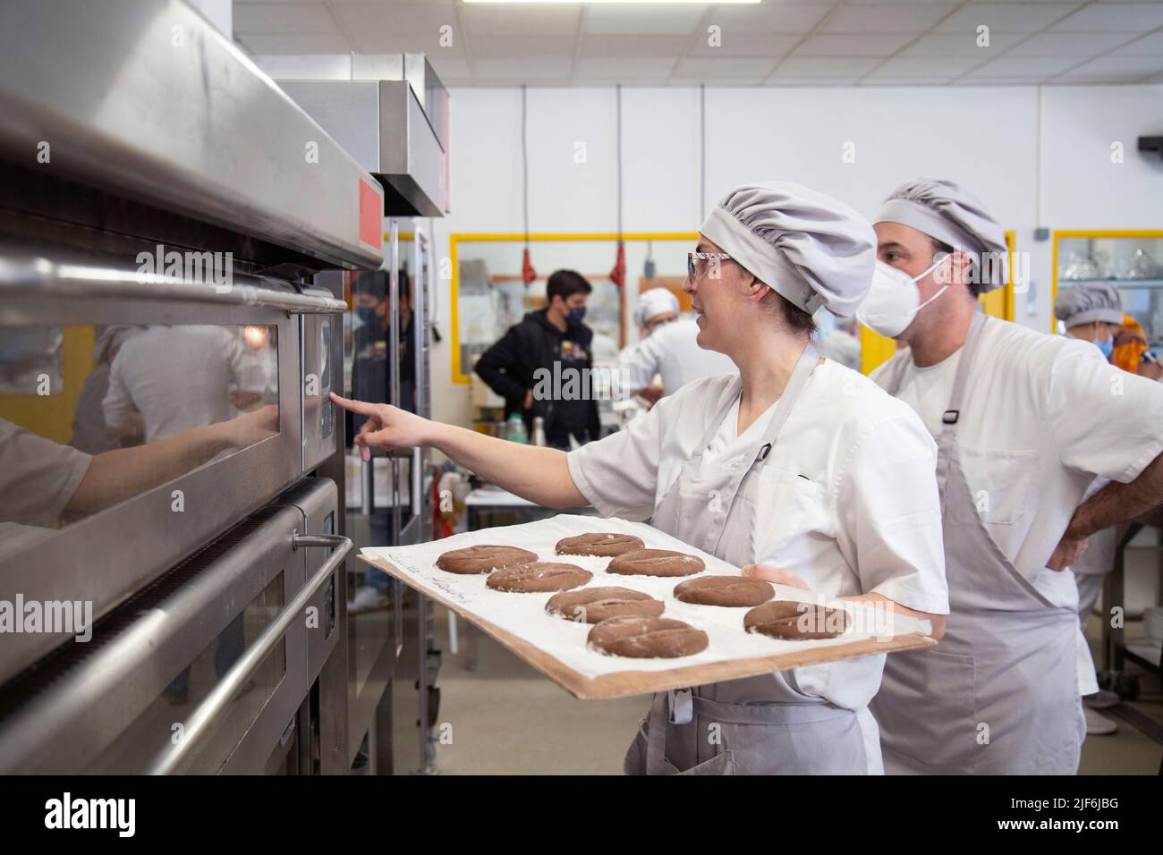 Side view of female baker in uniform with tray of bread dough turning ...