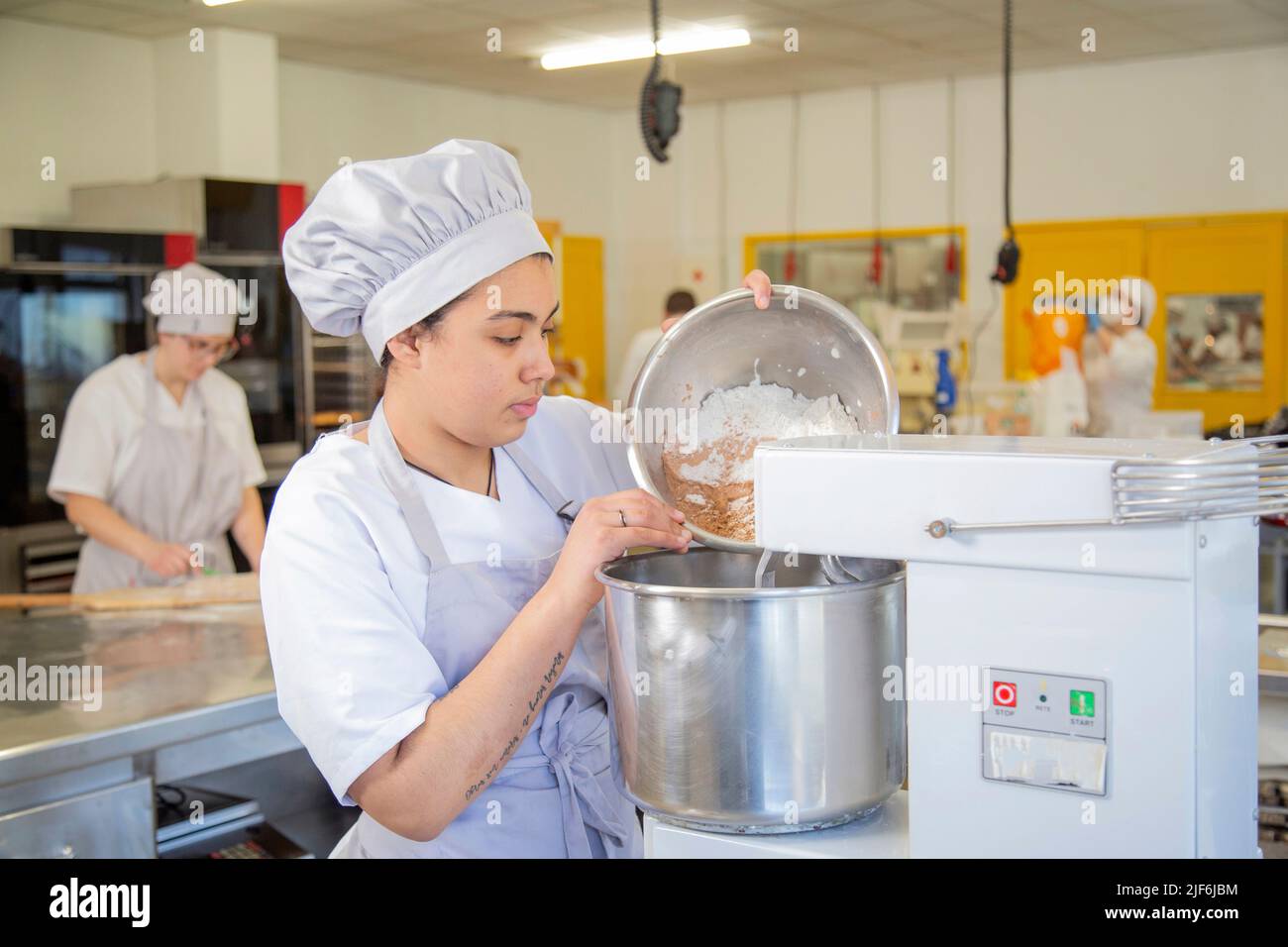 Side view of female baker in uniform pouring ingredient into bowl of ...