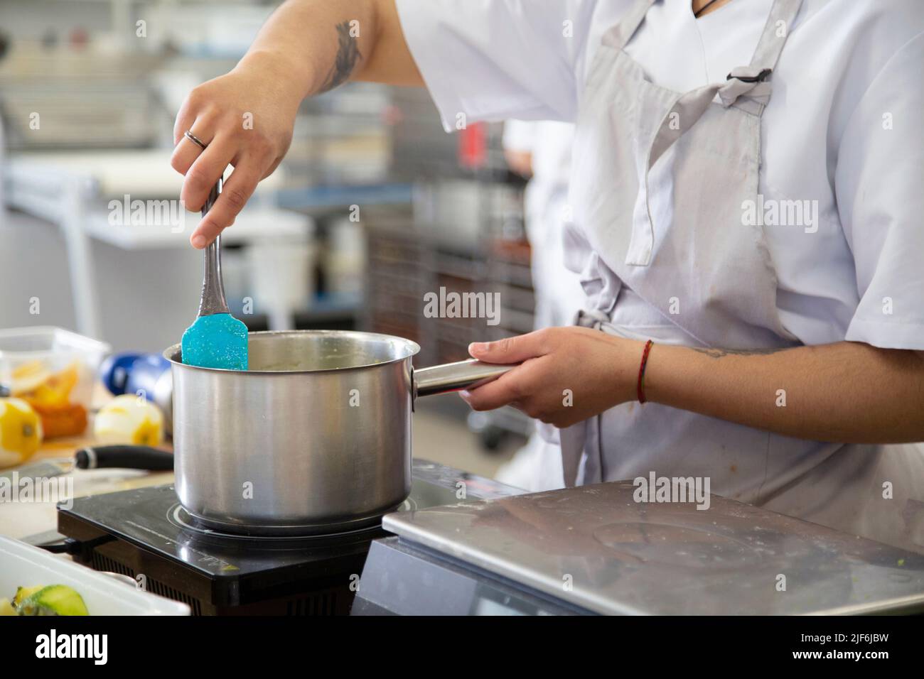 Crop anonymous female cook in uniform stirring ingredients in saucepan ...