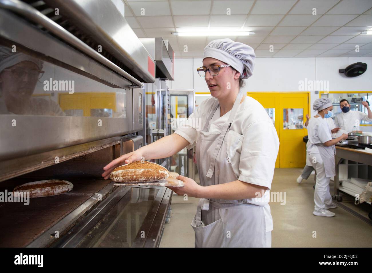 Side view of focused female baker taking out freshly baked bread from ...