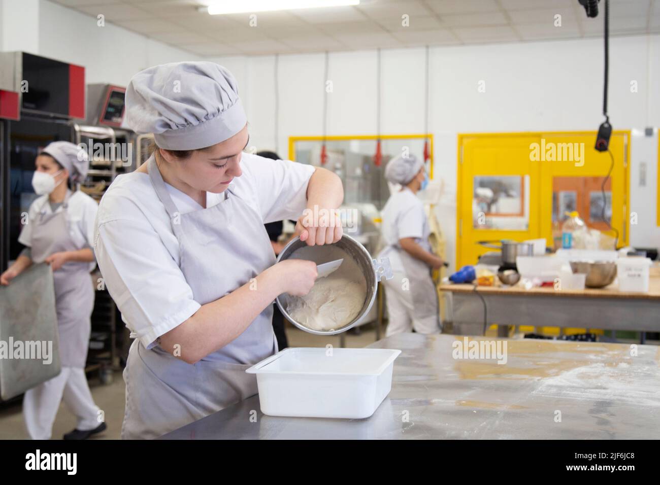 Side view of female baker in uniform putting raw dough from bowl into ...