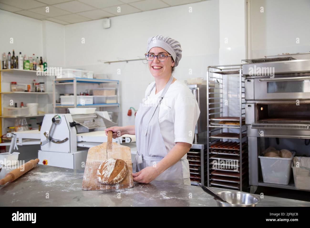 Cheerful female baker in uniform showing tasty baked bread loaf and ...