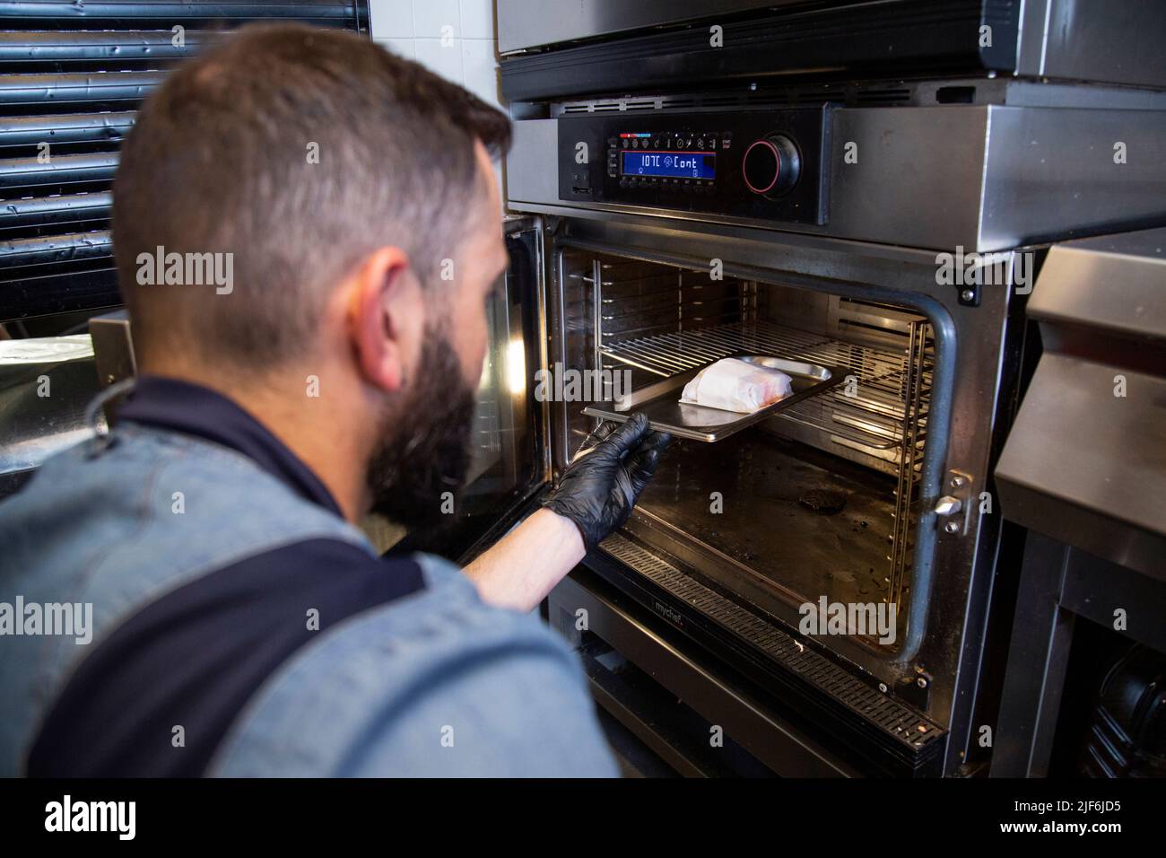 Chef placing wrapped stuffed meat on baking tray in oven at commercial ...