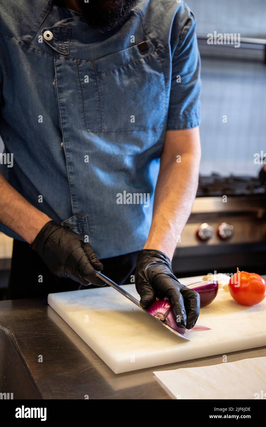 Male chef slicing onion and tomato on cutting board in restaurant Stock ...