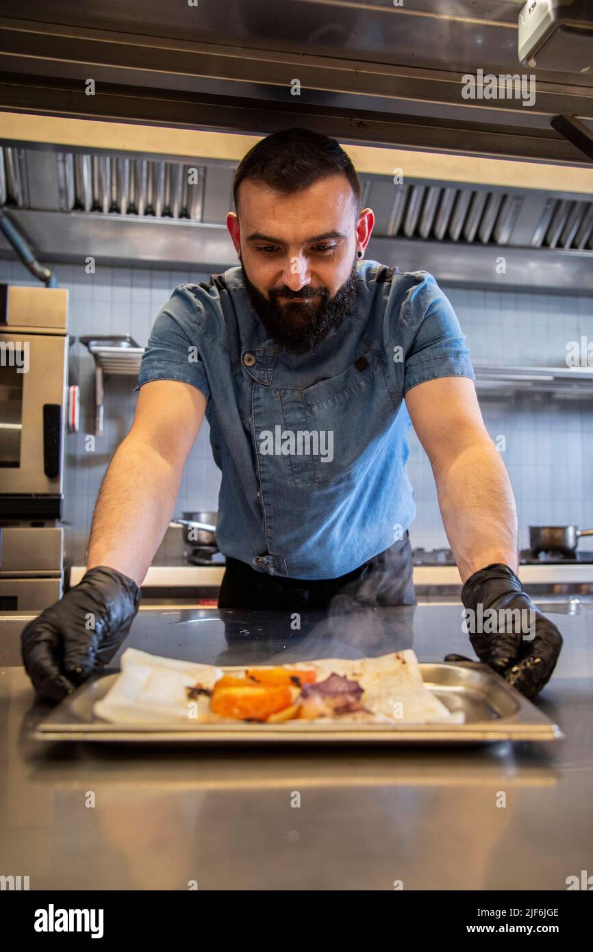 Happy male chef with prepared food in baking tray at industrial kitchen ...