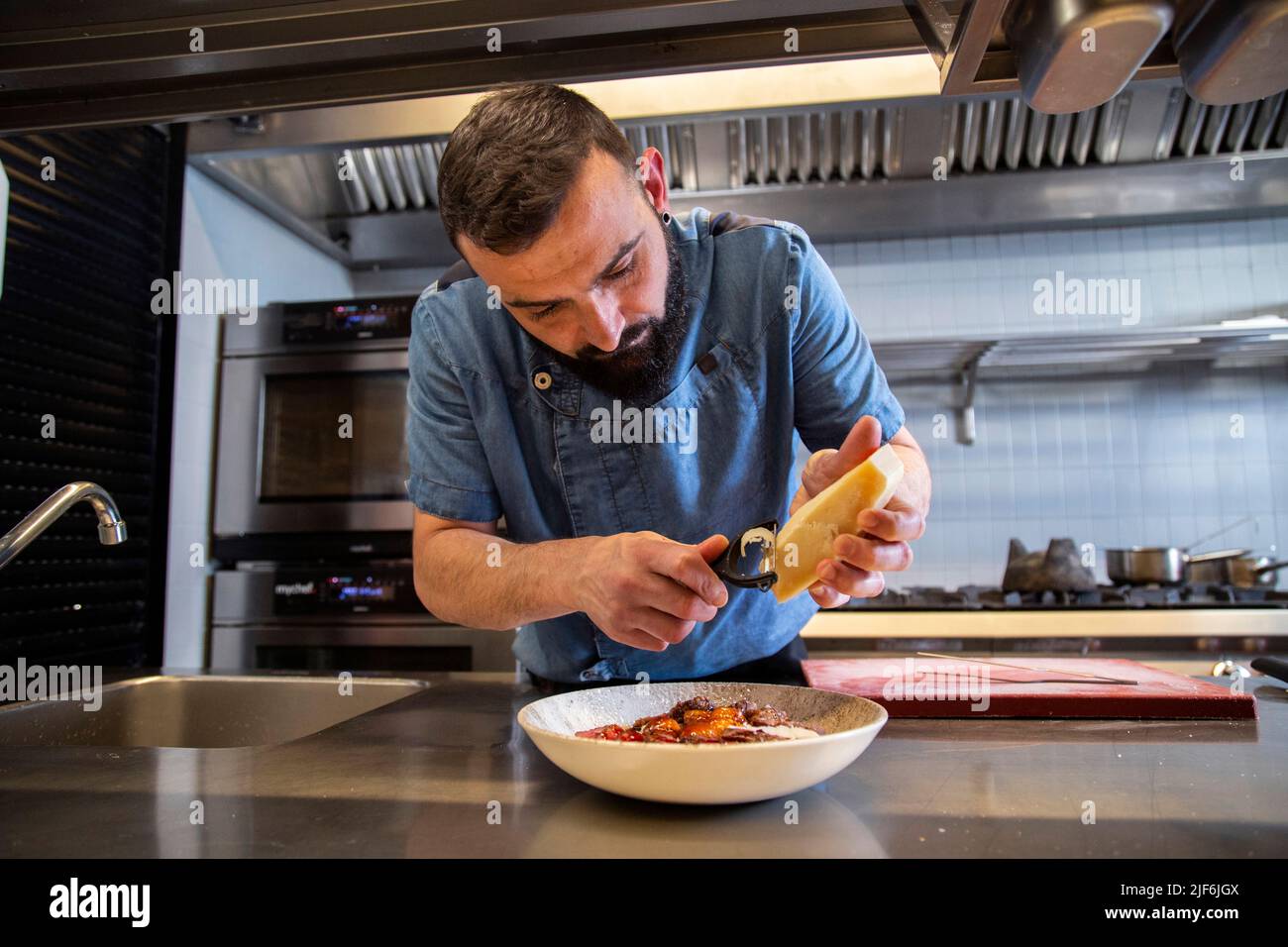 Chef garnishing dish of steak with cheese at kitchen counter in ...