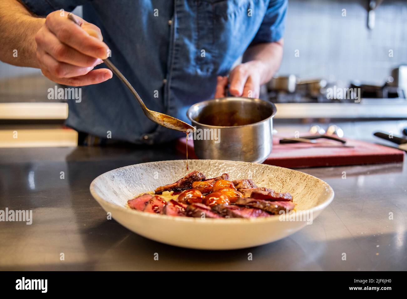 Crop Caucasian chef pouring sauce on beef in bowl at commercial kitchen ...