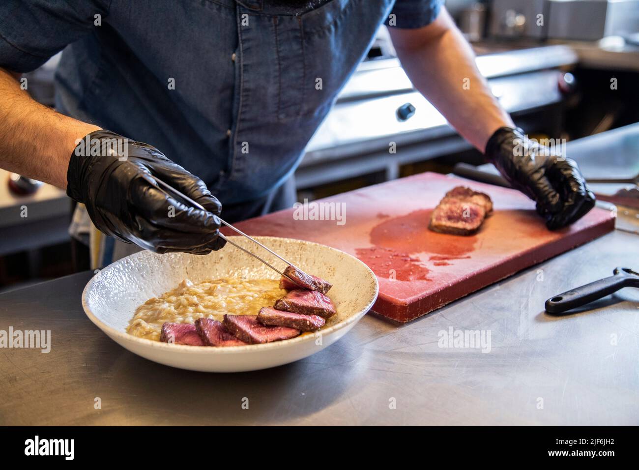 Male chef placing steak slices in bowl on counter in restaurant kitchen ...