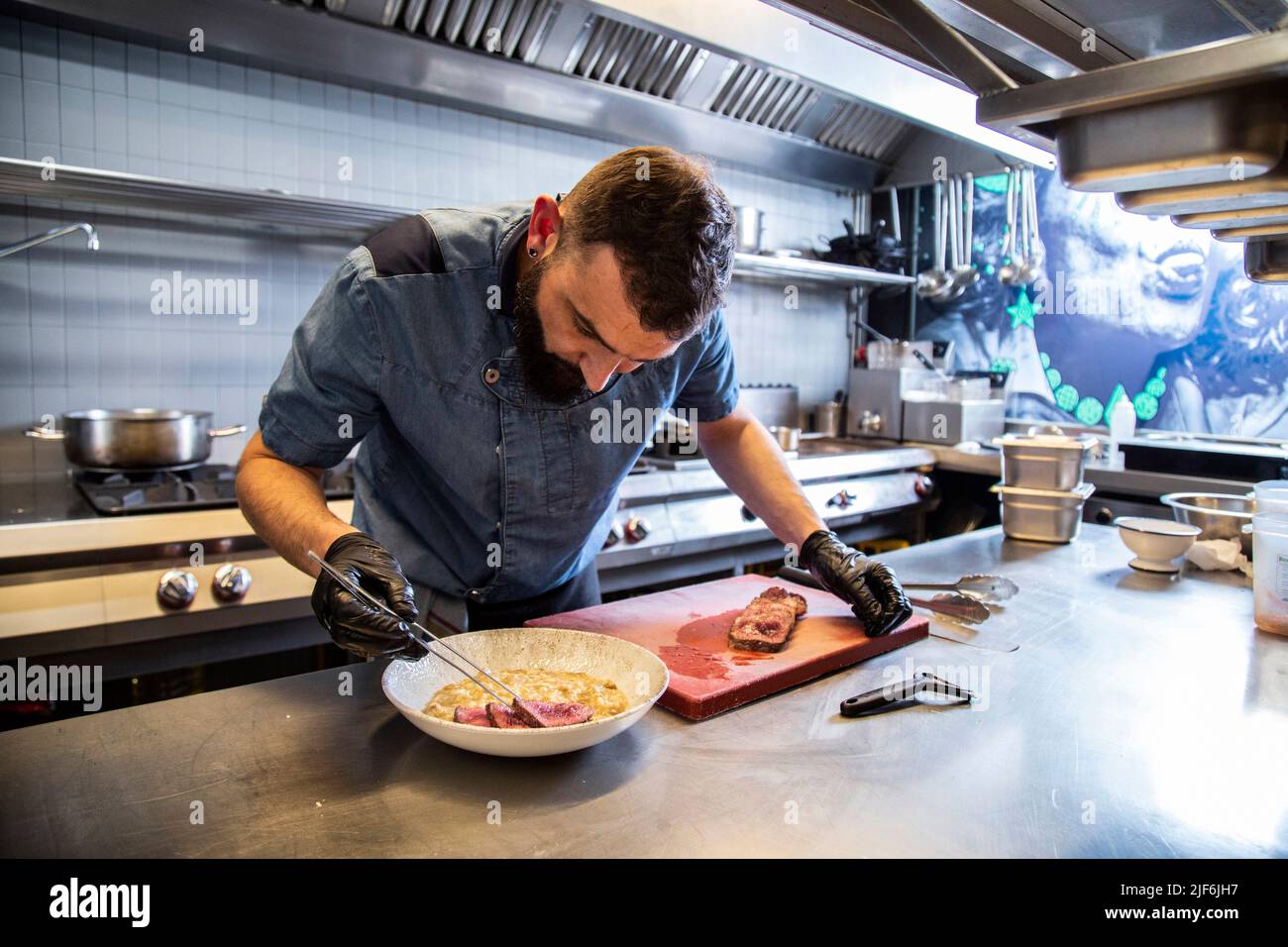 Male chef placing steak slices in bowl on counter in restaurant kitchen ...