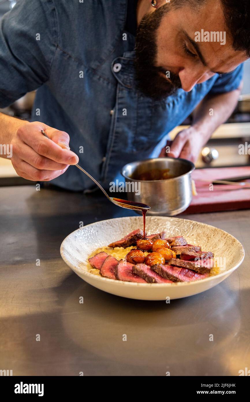 Crop Caucasian chef pouring sauce on beef in bowl at commercial kitchen ...