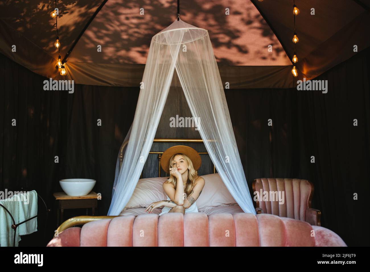 Serene female with stylish hat sitting on comfortable bed with ...