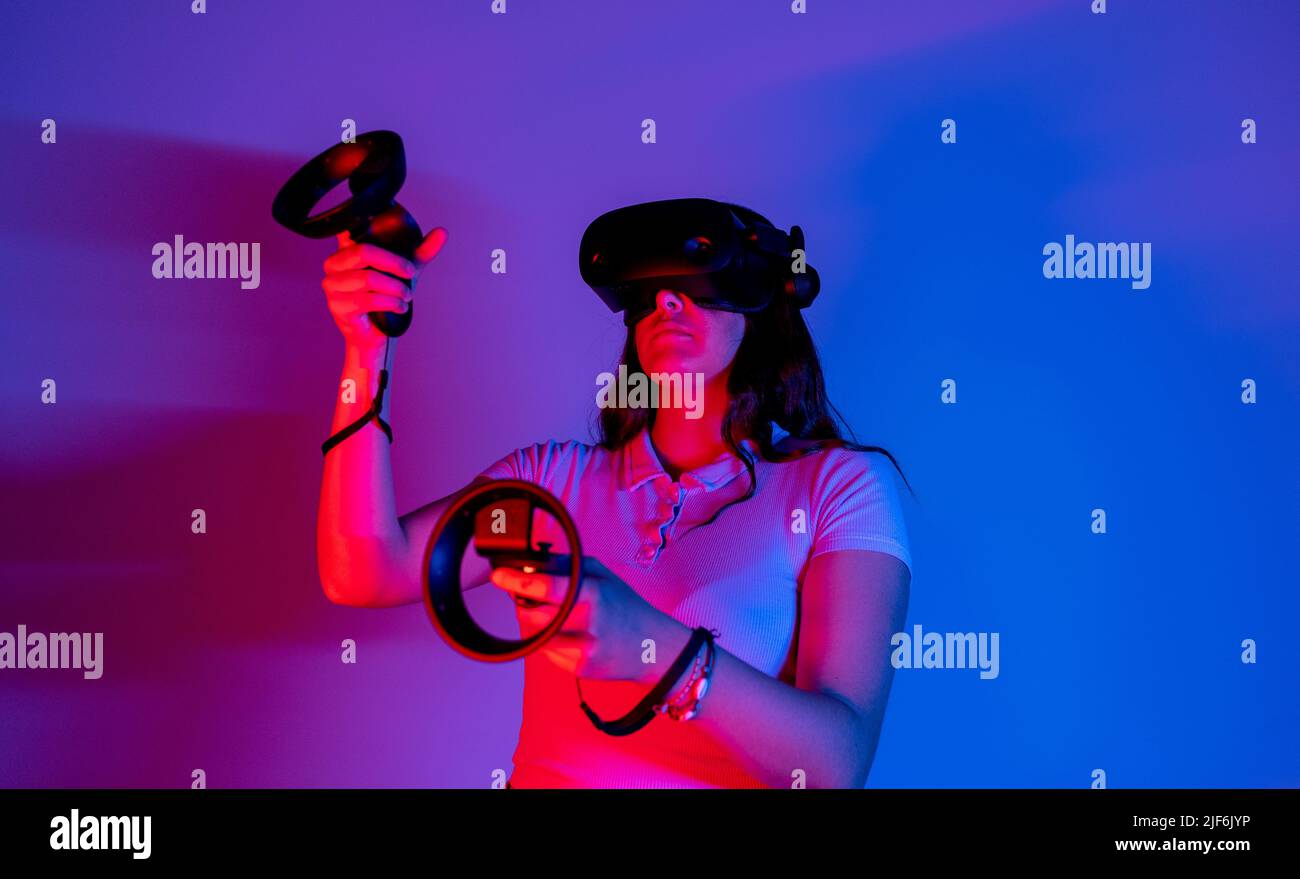 Woman in modern VR goggles with remote controllers playing videogame ...