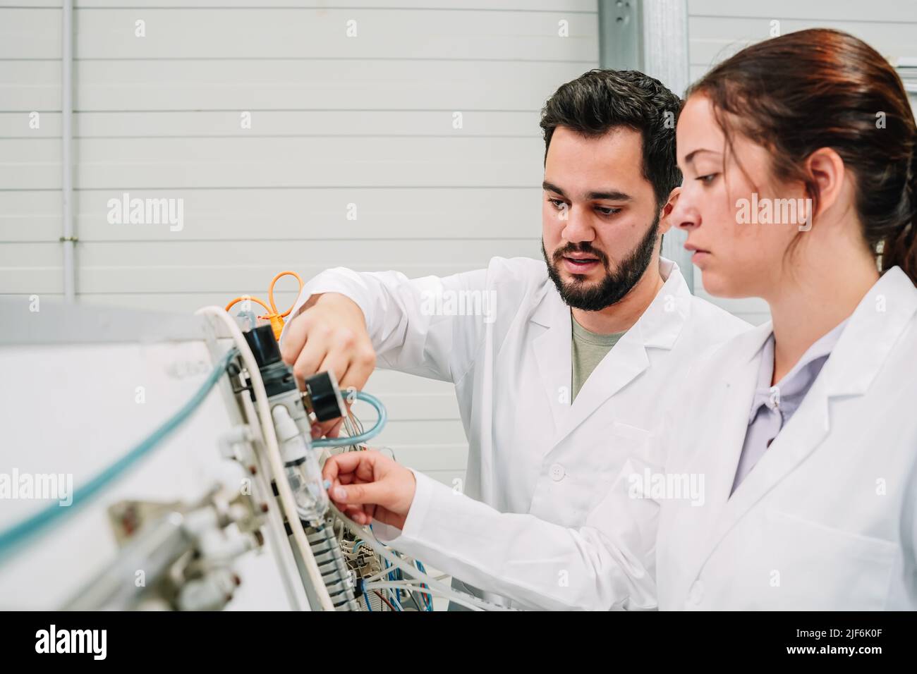 Side view of focused scientists in white uniforms setting up modern ...
