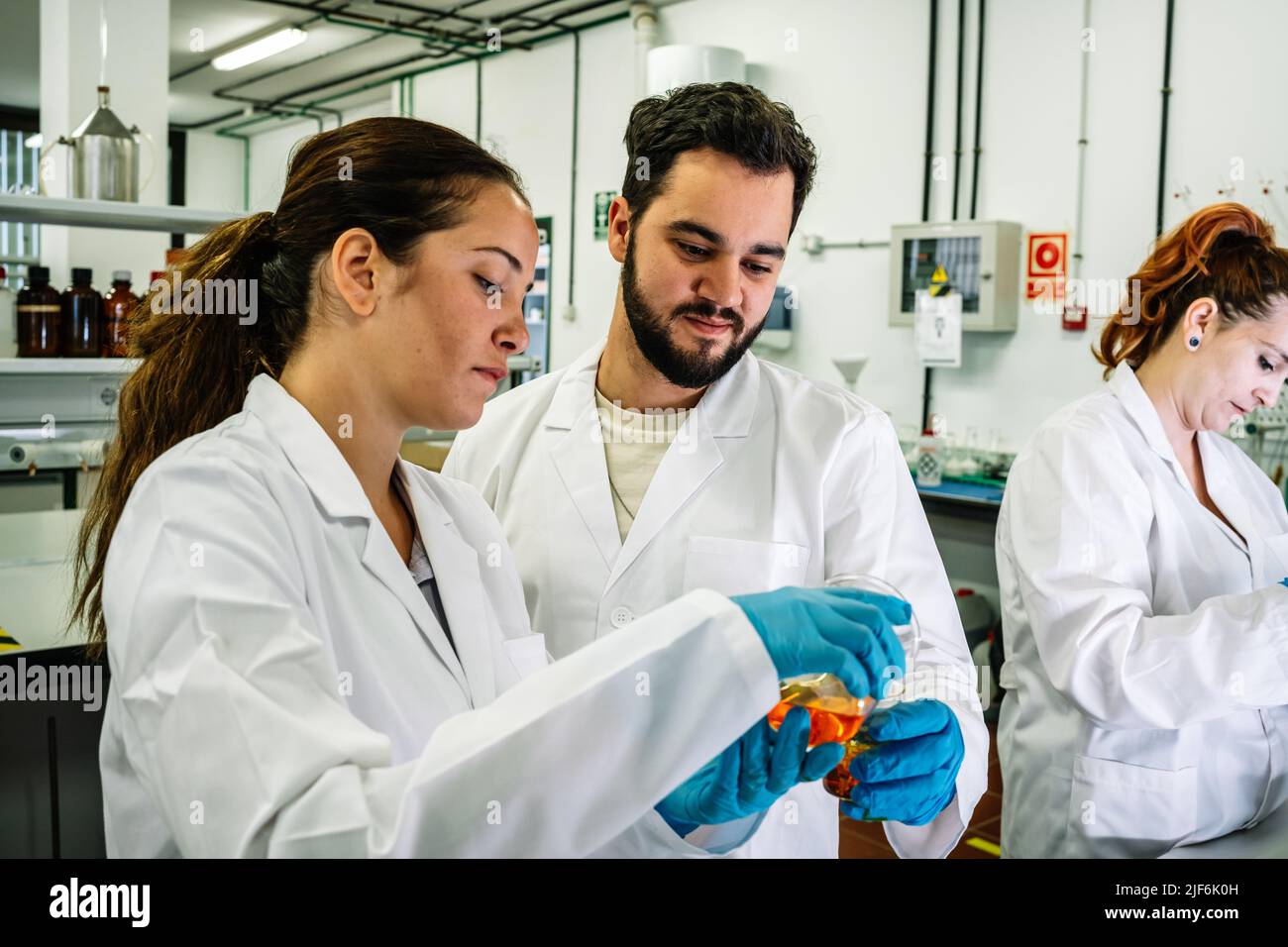 Side view of cheerful chemists in medical uniform pouring chemical ...