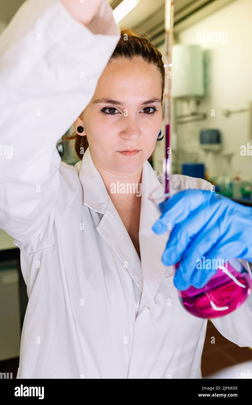 Concentrated female scientist in medical uniform pouring colorful chemical liquid from pipette ...