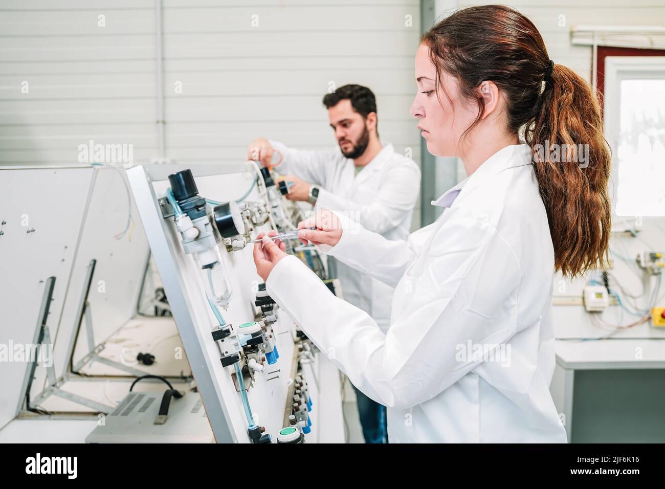 Side view of focused scientists in white uniforms setting up modern ...