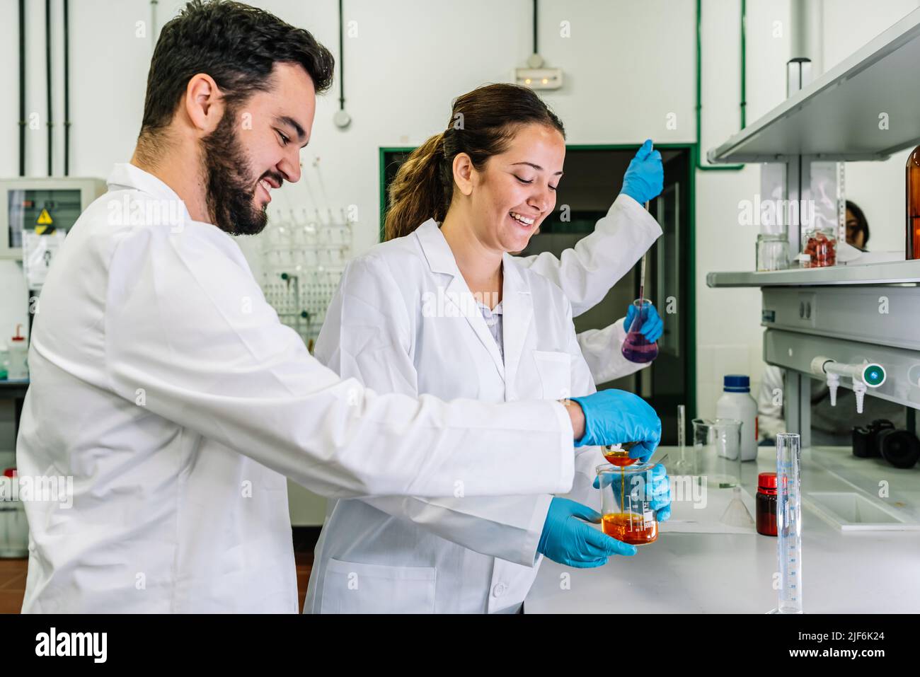 Side view of cheerful chemists in medical uniform pouring chemical ...